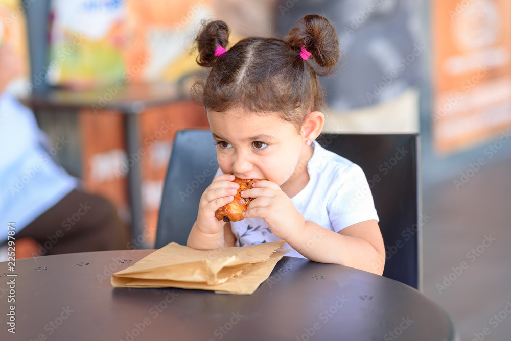 Fotografia do Stock: Kid devours croissant. Cute Little girl having ...
