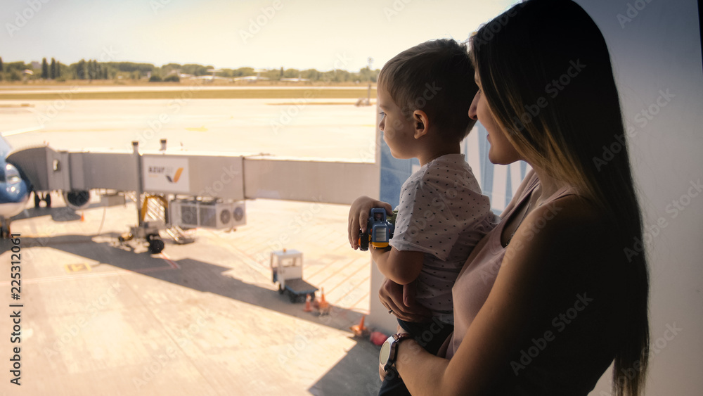 Toned image of young mother holding her toddler son and showing ...