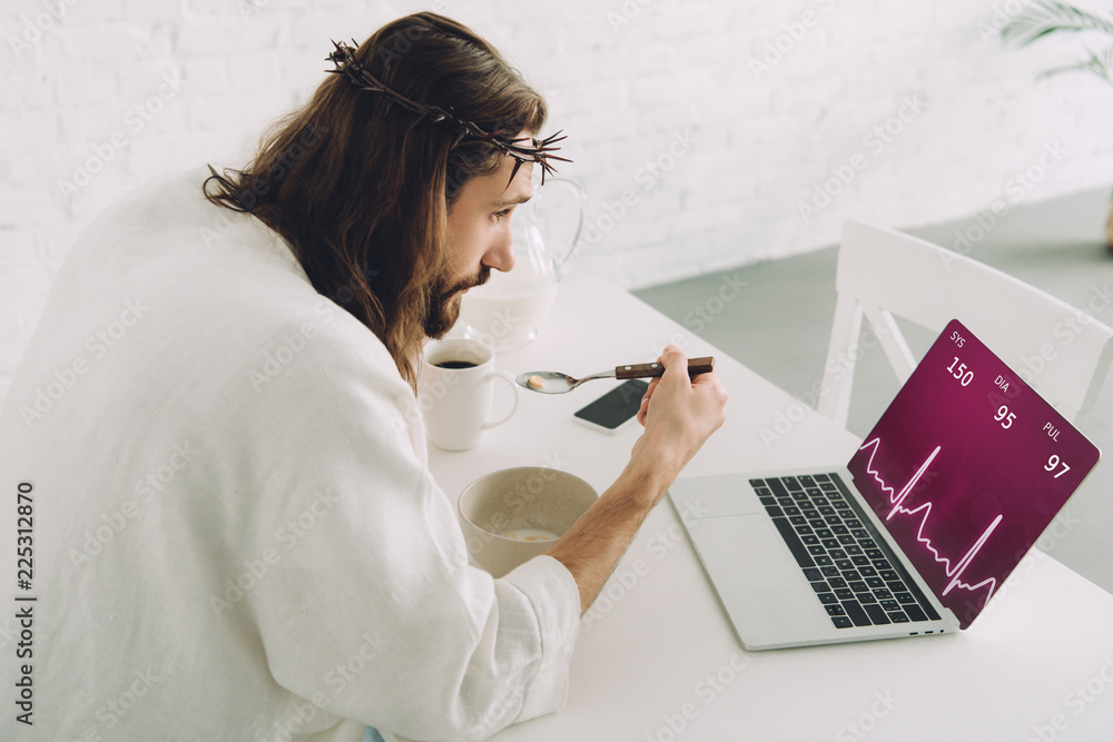 concentrated Jesus eating corn flakes on breakfast at table with laptop ...