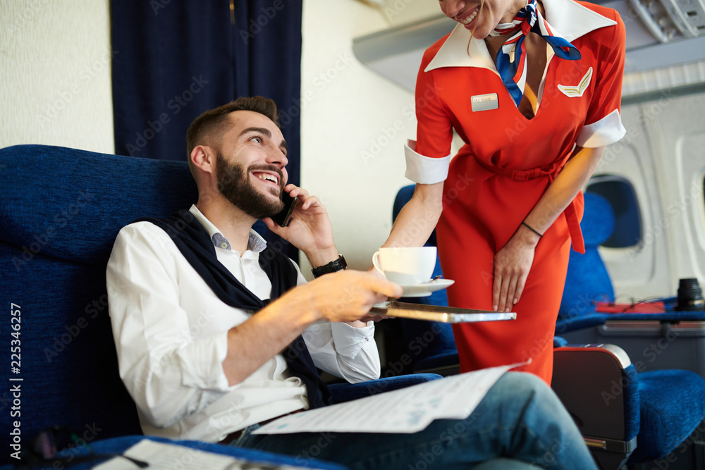 Portrait of smiling flight attendant serving coffee to handsome ...