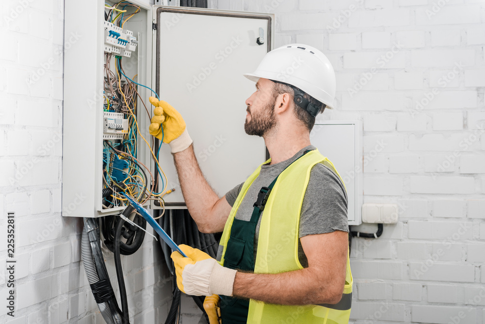 side view of electrician holding clipboard and checking wires in ...
