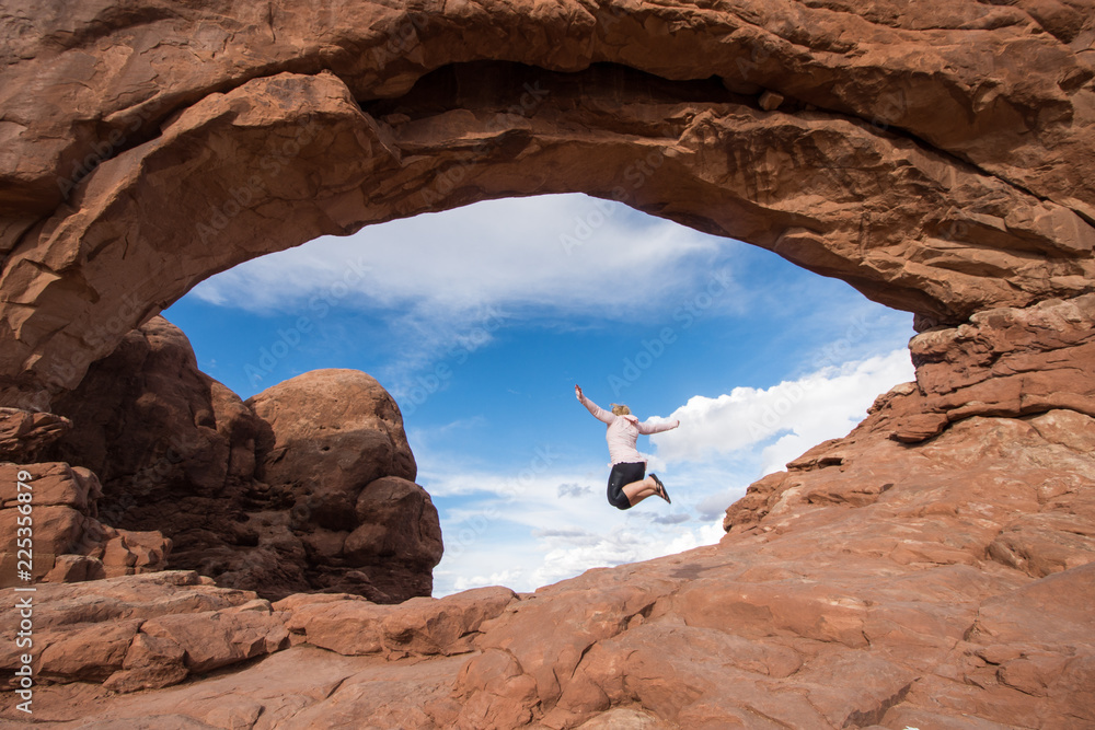 Adult woman jumps inside of Skyline Arch in Arches National Park, in ...