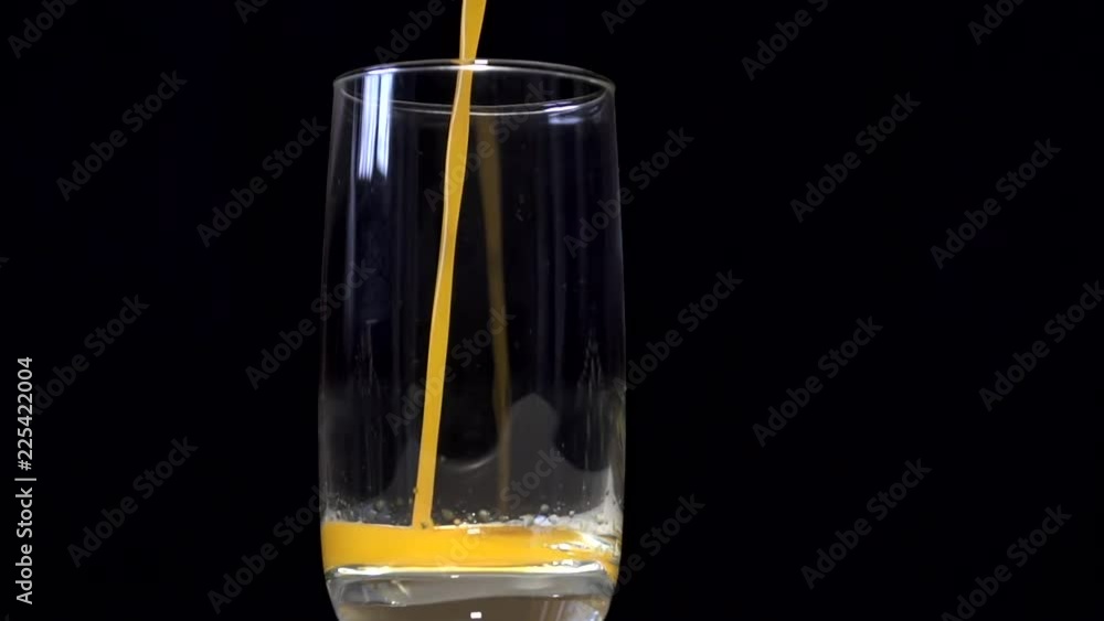 Pouring orange and yellow juice into a glass beaker. Behind the black ...