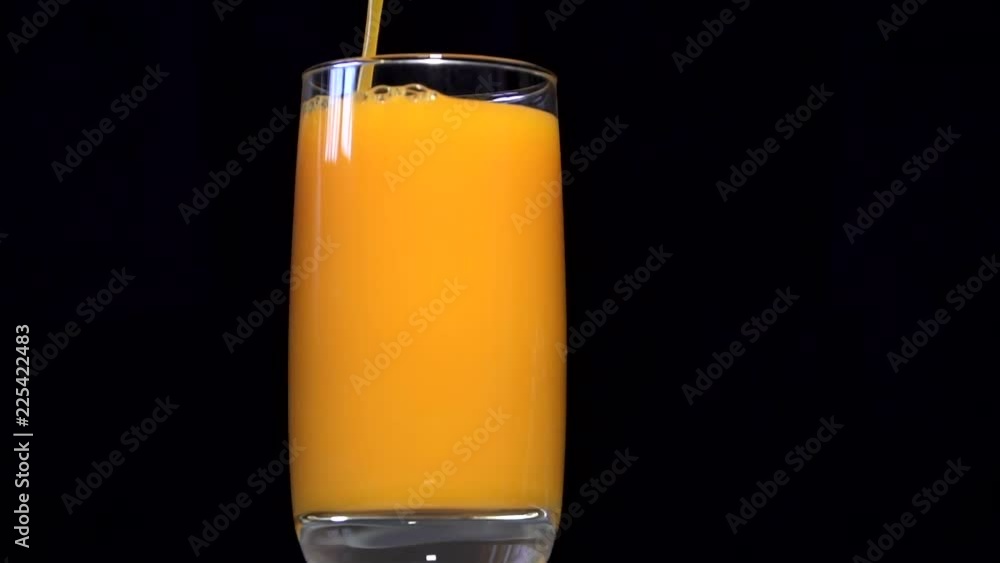 Pouring orange and yellow juice into a glass beaker. Behind the black ...