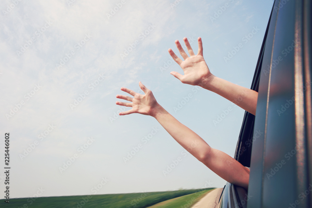 Boy putting his heads and hands out of the car window on a roadtrip ...
