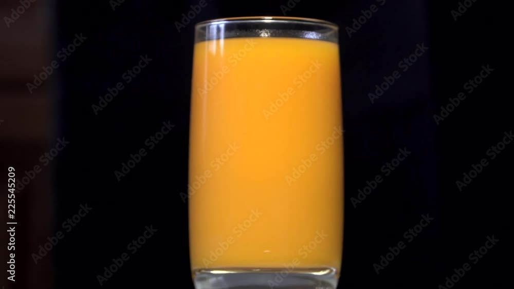 Pouring orange and yellow juice into a glass beaker. Behind the black ...