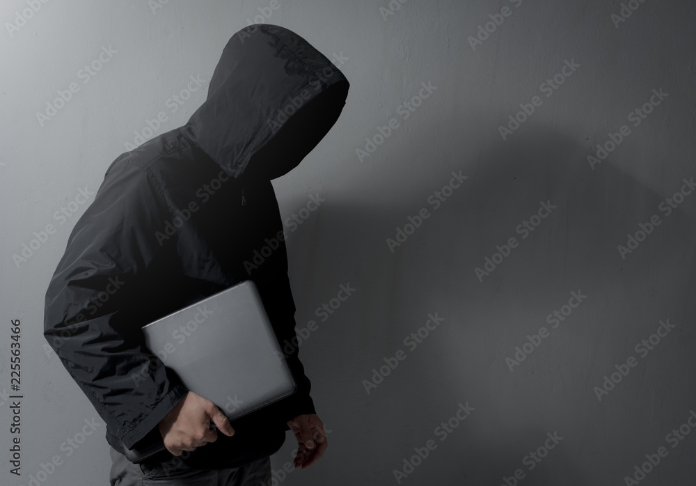 Hacker with hidden face in a hoodie holding a laptop against white ...