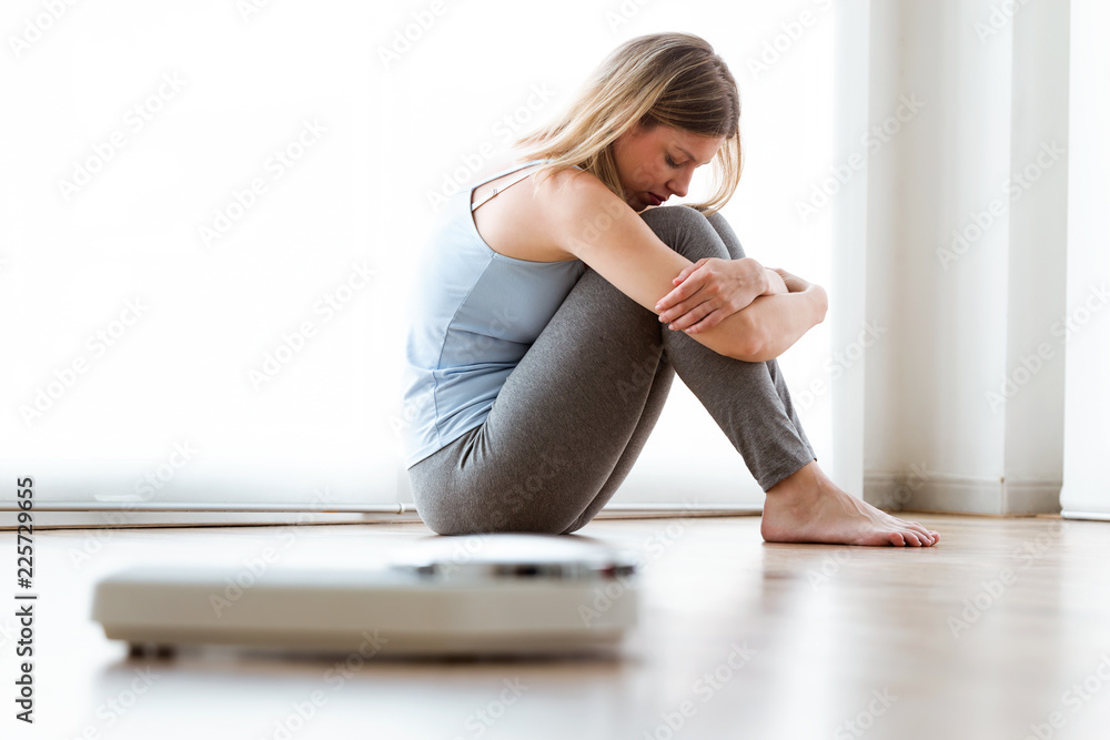 Frustrated young sad woman after seeing her weight on the scale at home ...