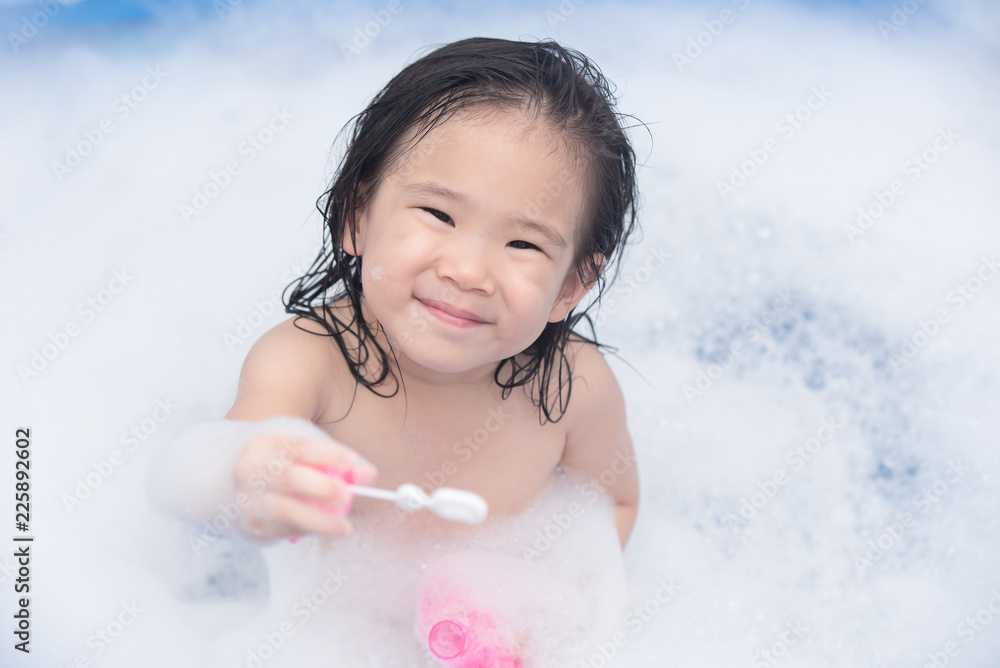 Happy little girl playing in bath tube with foam bubbles. Little child ...