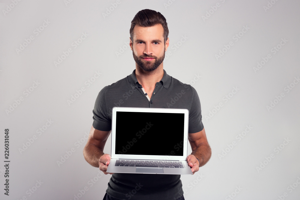 Your new laptop. Handsome young man looking at camera and showing his ...