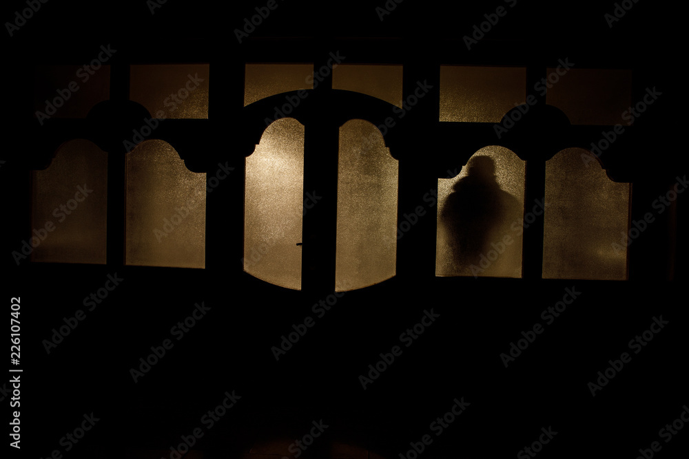 Silhouette of an unknown shadow figure on a door through a closed glass ...