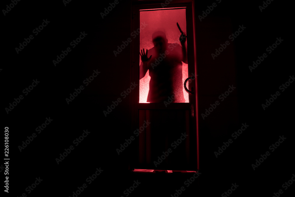 Silhouette of an unknown shadow figure on a door through a closed glass ...