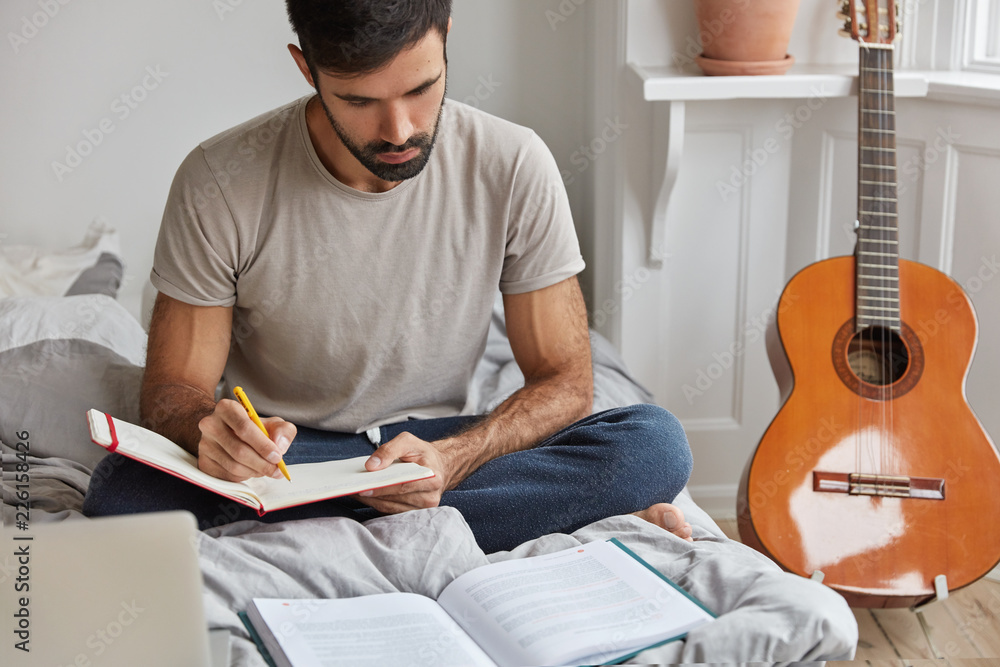 Cropped shot of serious unshaven young guy concentarted on writing ...