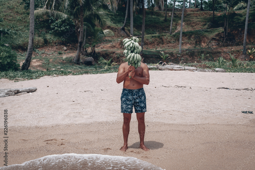 Sports man standing on the beach and holding a lot of bananas Green ...