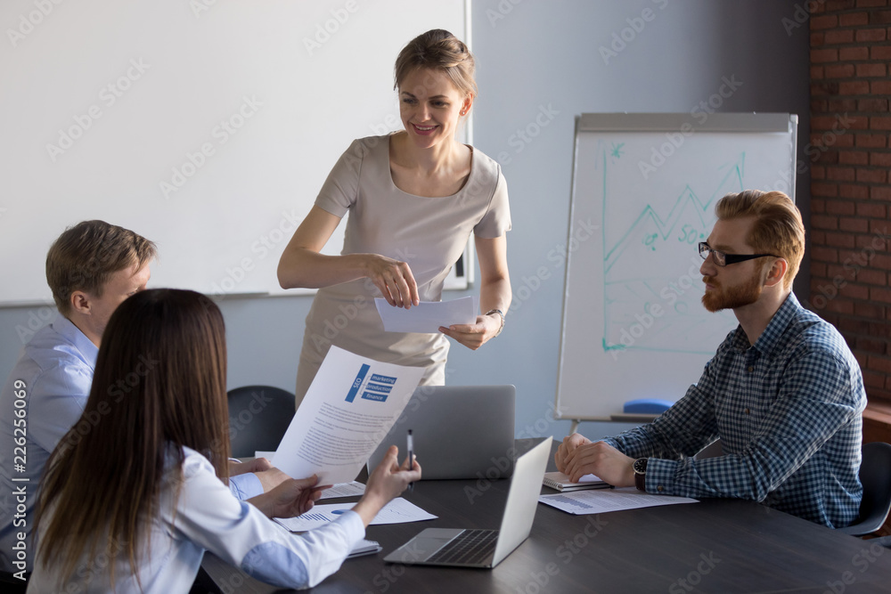 Smiling female ceo leader giving team members papers financial report ...