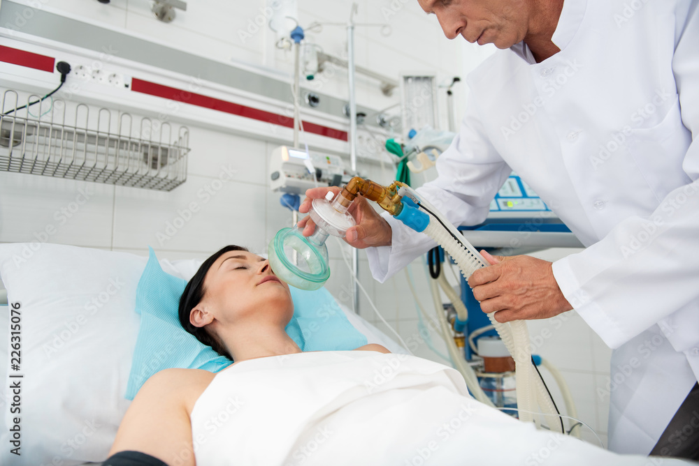 Female patient lying in hospital bed and getting mechanical ventilation ...