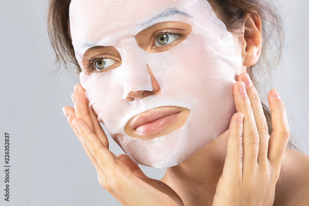 Woman with a sheet moisturizing mask on her face isolated on gray ...