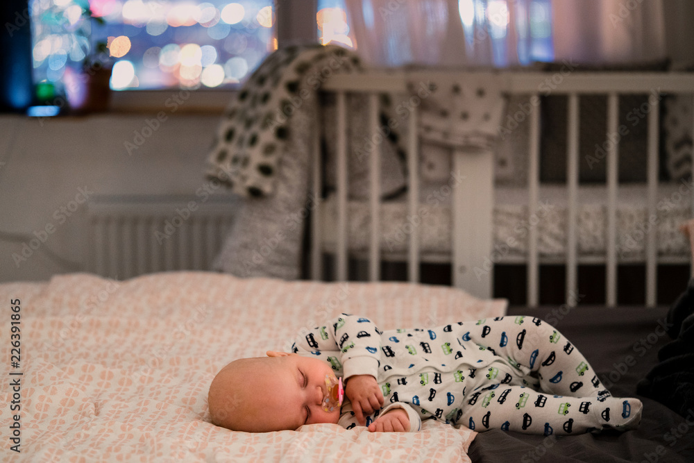 Adorable baby sleeping in a larger bed at night in pajamas. Bed linen ...