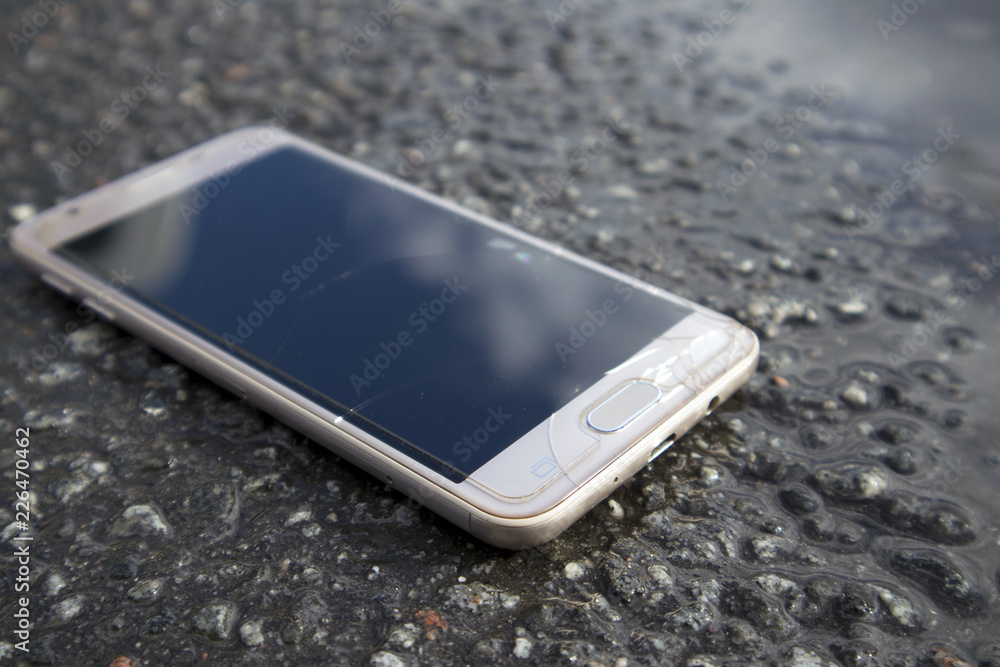 Modern smart phone with cracked screen glass lying in a puddle on the ...
