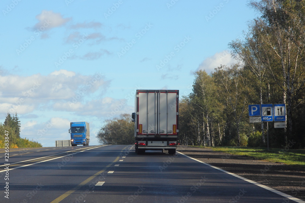 White truck with a semi-trailer rides on a suburban highway road on a ...