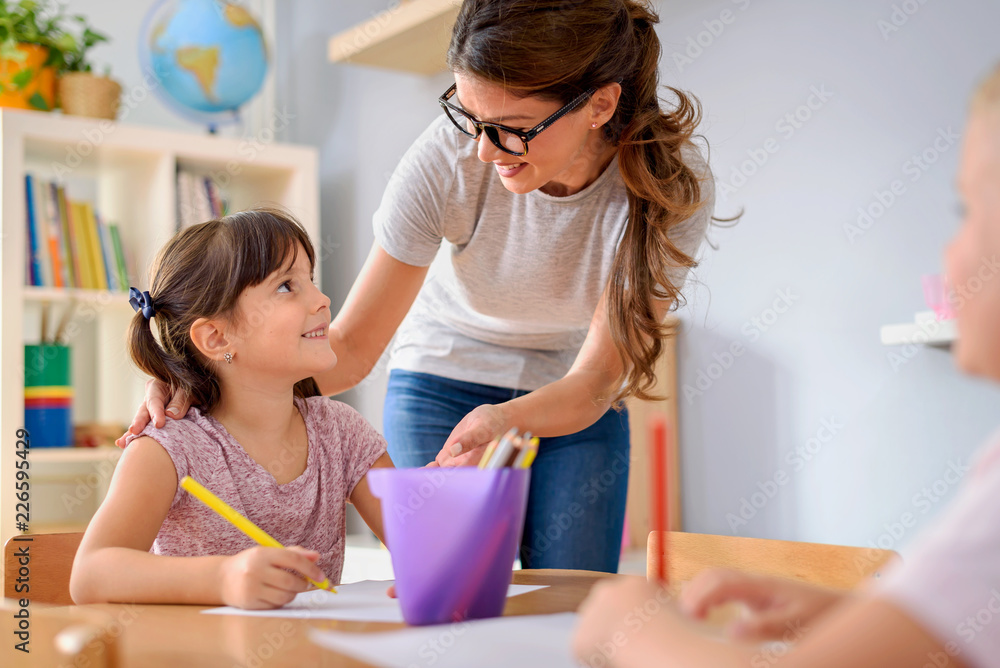 Preschool teacher assisting children with their drawings. Early ...