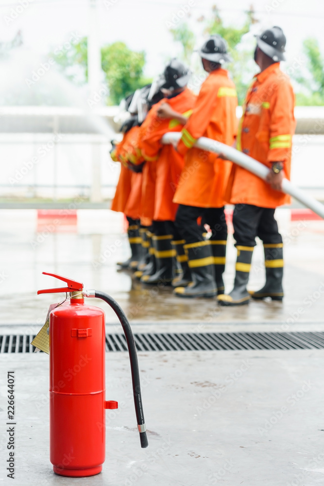 Red tank of fire extinguisher, foreground is firefighter spraying high ...