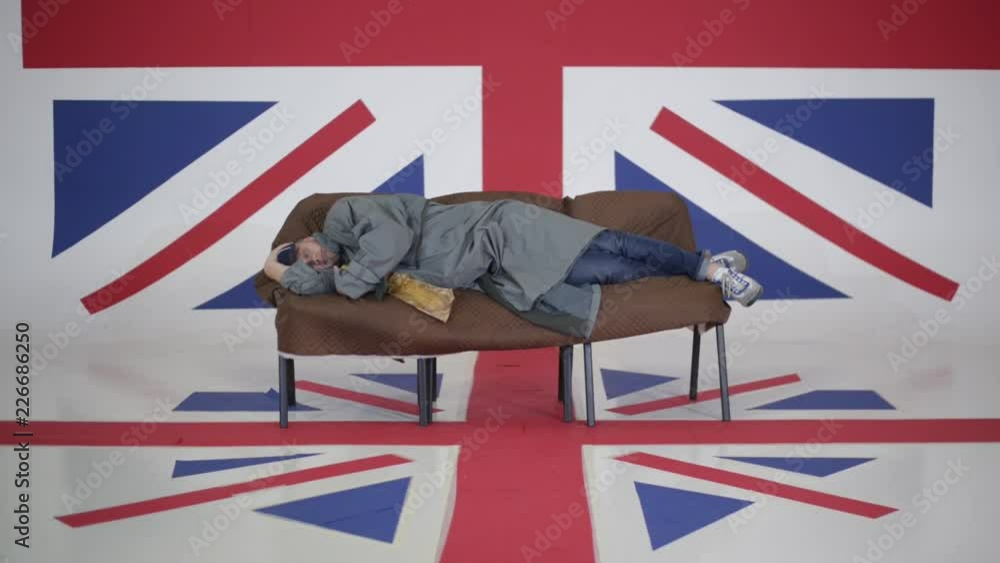 Homeless looking man in blue cap and long grey coat is lying on small ...