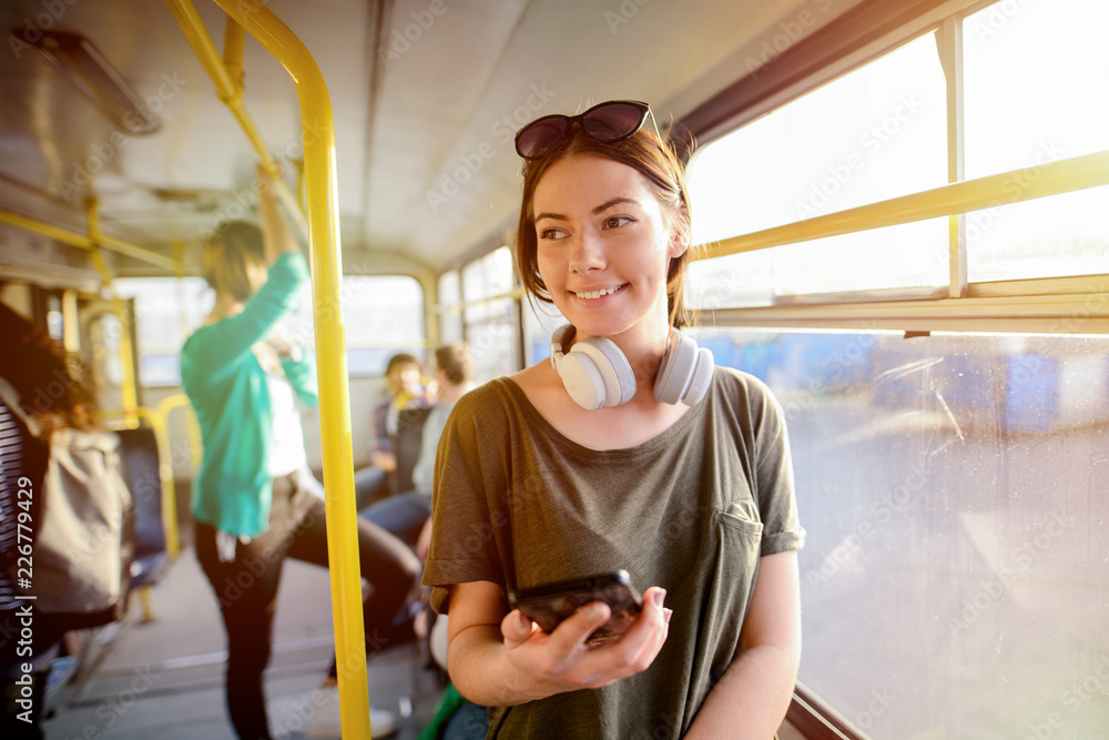 Modern smiling cute girl standing in a bus with headphones around her ...