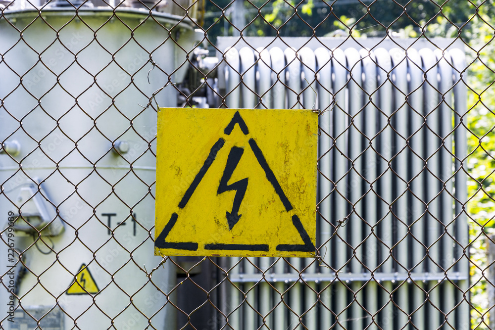 warning sign of electricity, high voltage, hanging on the fence around ...