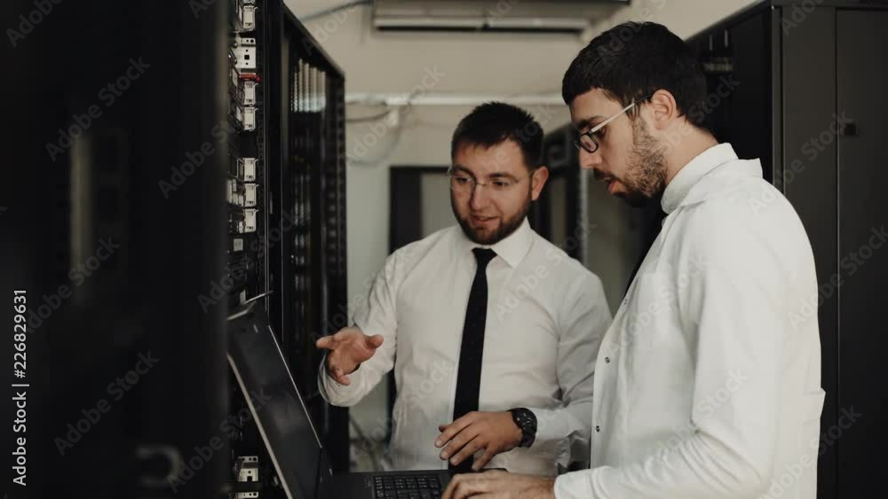 Vidéo Stock Two IT engineers are working in a data center with rows of ...