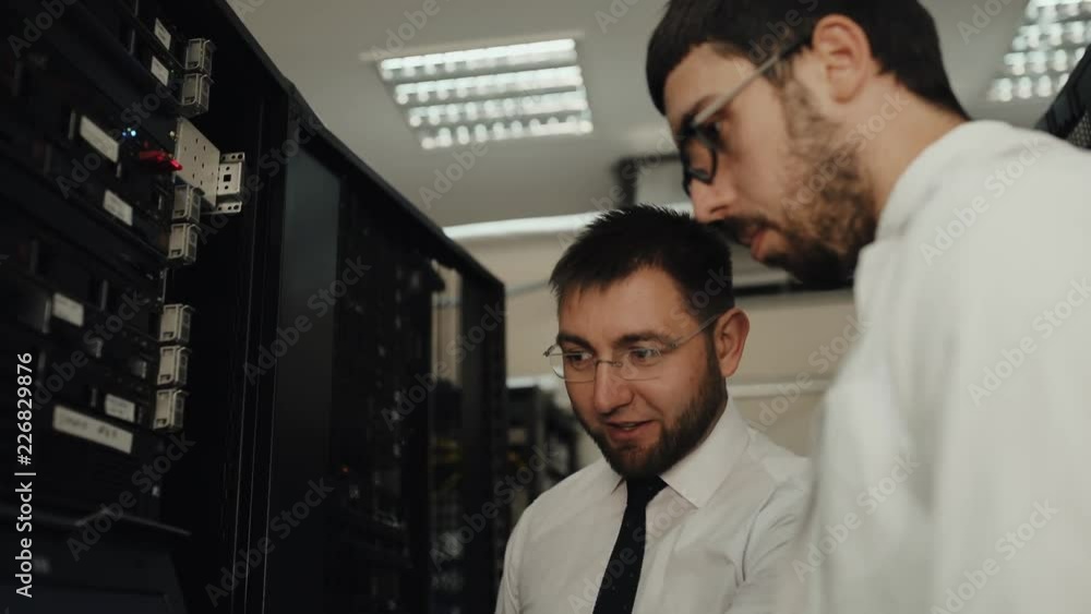 Vidéo Stock Two IT engineers are working in a data center with rows of ...