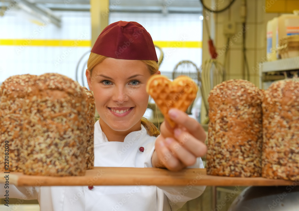 A young woman takes up her work in a bakery. She poses for the camera ...