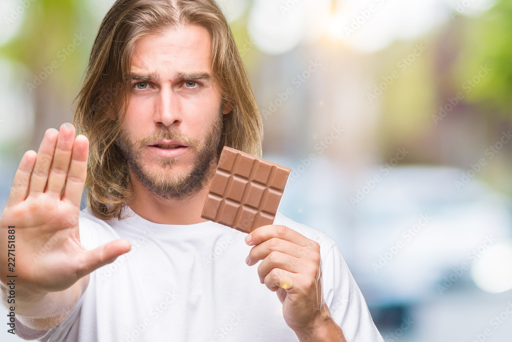 Young handsome man with long hair eating chocolate bar over isolated ...