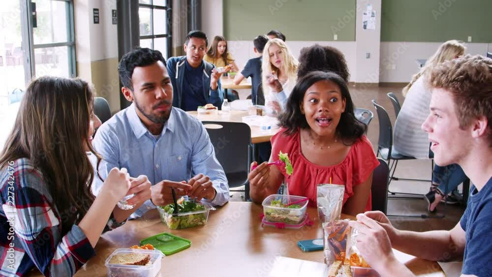 Teacher And Students Eating Lunch In High School Cafeteria During ...