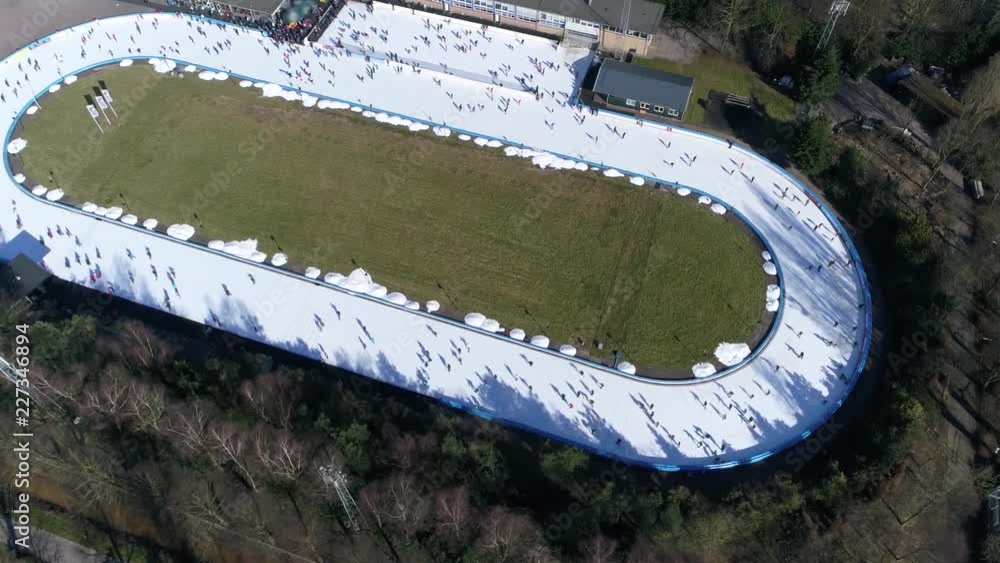Aerial flight towards oval shaped ice rink frozen body of water where ...