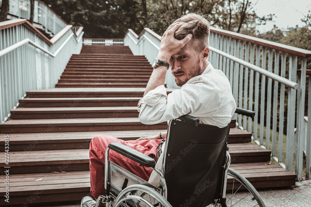 Stairs and wheelchair. Unhappy disabled young man feeling shocked and ...
