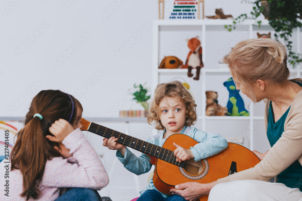 Cute little boy learning how to play guitar during lesson in preschool ...