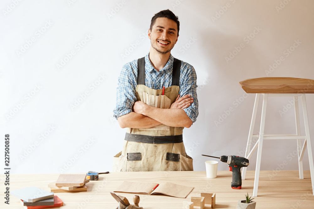 Skilled craftsman in apron looking up from his work and smiling at ...