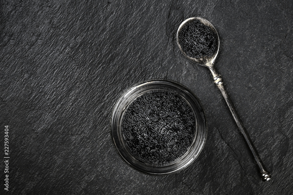 Black fish roe in a jar and in a spoon, shot from the top on a black ...