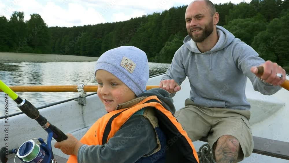 Father and his little son with rod floating in a rowing boat on the ...