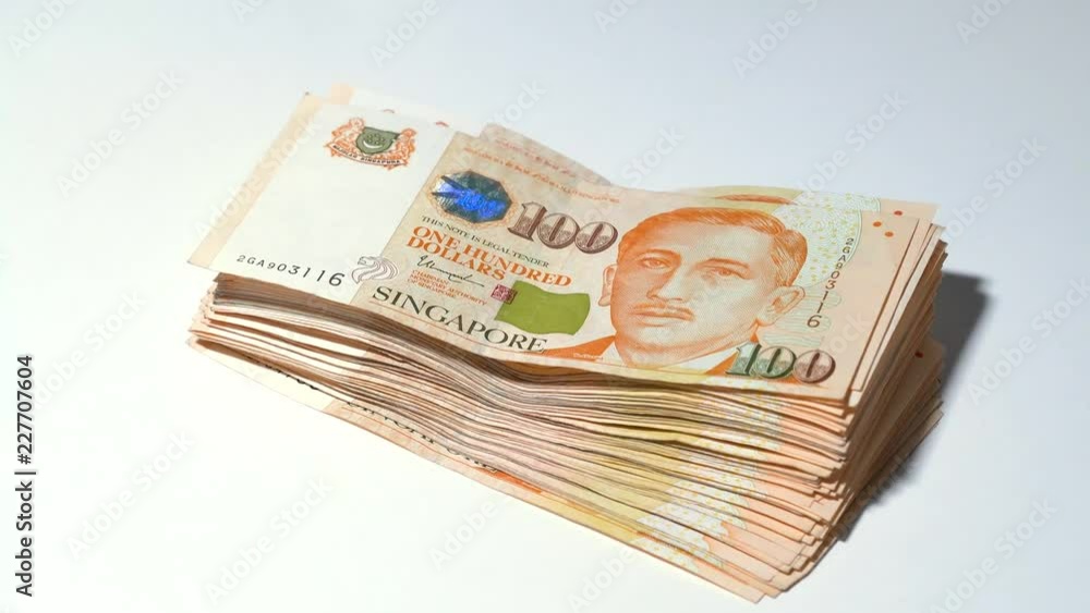 Panning in from the left to reveal a stack of SGD 100 dollar bill ...