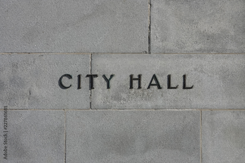 Metal letters reading CITY HALL are shown affixed to a concrete ...