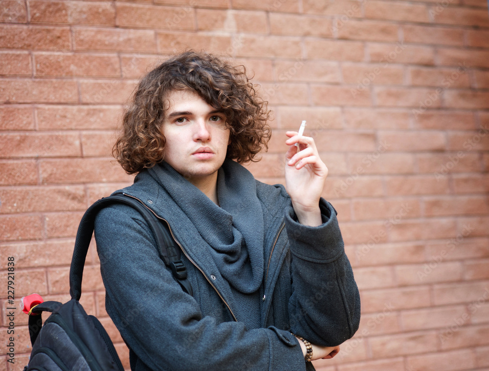 Portrait of a handsome man standing against brick wall and smoking a ...