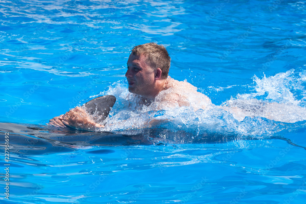 A young man is riding dolphin, boy swimming with dolphin in blue water ...