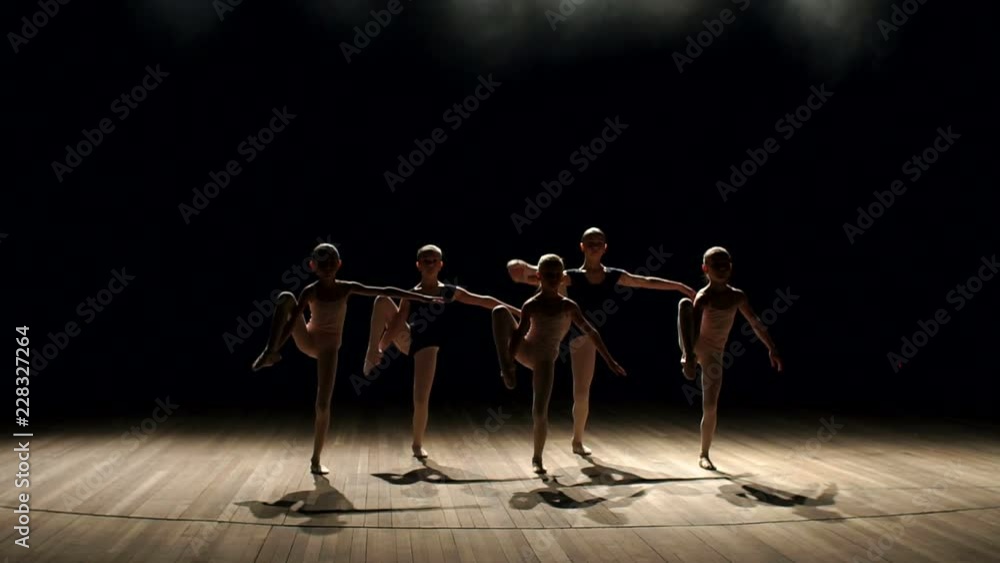 Five ballerinas show a complex gymnastic exercise on stage in the dark ...