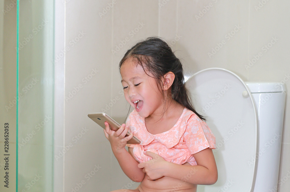 Close-up happy little Asian child girl sitting on toilet and playing ...