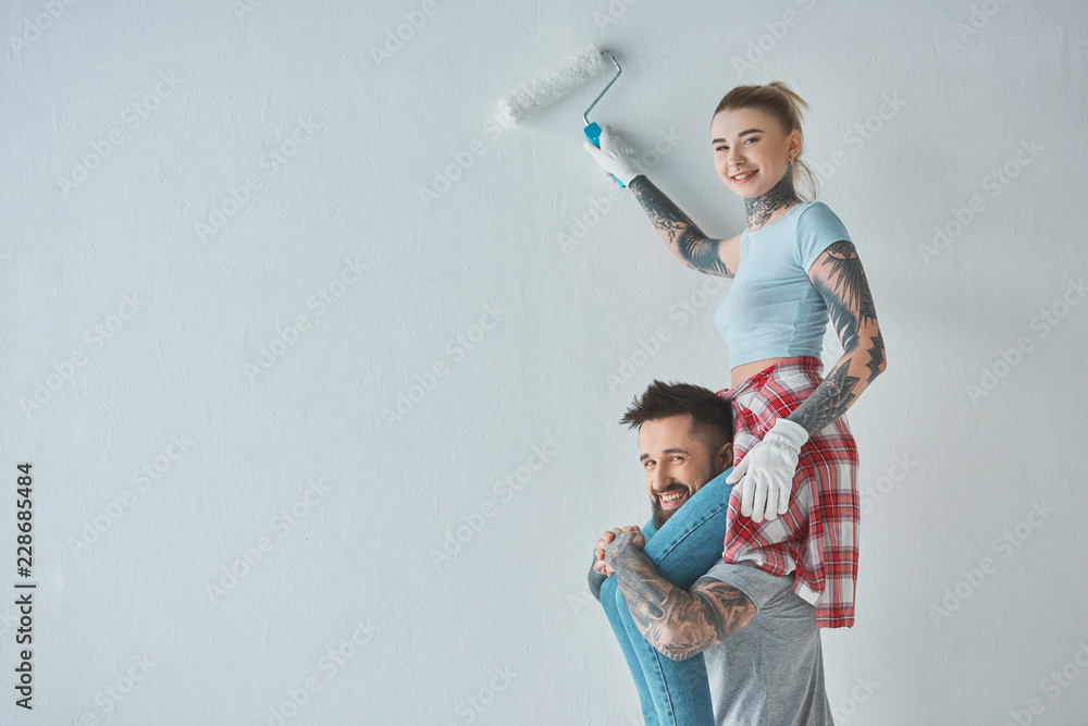smiling woman with roll paint brush sitting on boyfriends shoulders ...