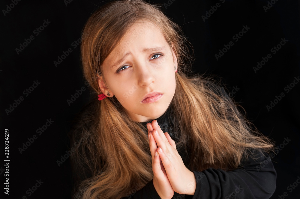 Beautiful young sad girl praying on a black background with hands in ...