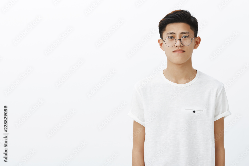 Charming young chinese guy in trendy glasses and t-shirt standing to ...