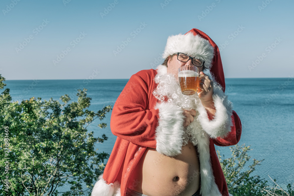 Fat man in glasses dressed as Santa drinking beer on the ocean. Funny, drunk and happy Stock ...